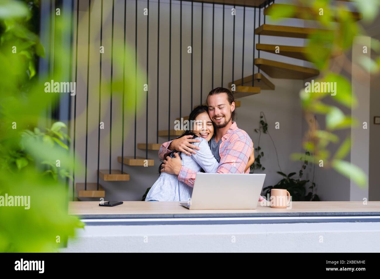 Young diverse couple hug and smile while sitting by a laptop together ...