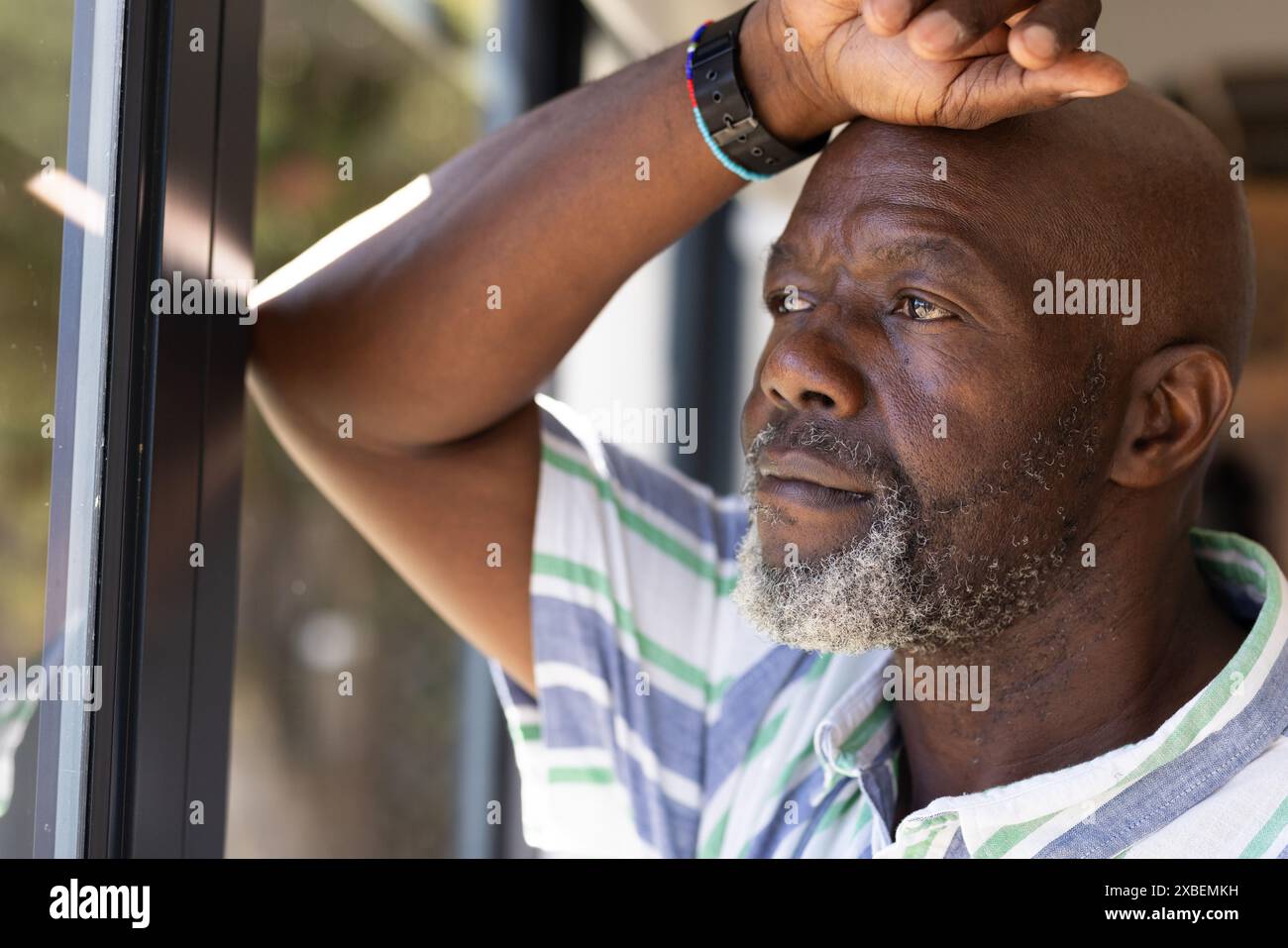 Mature African American man gazing thoughtfully out of window. Sunlight ...