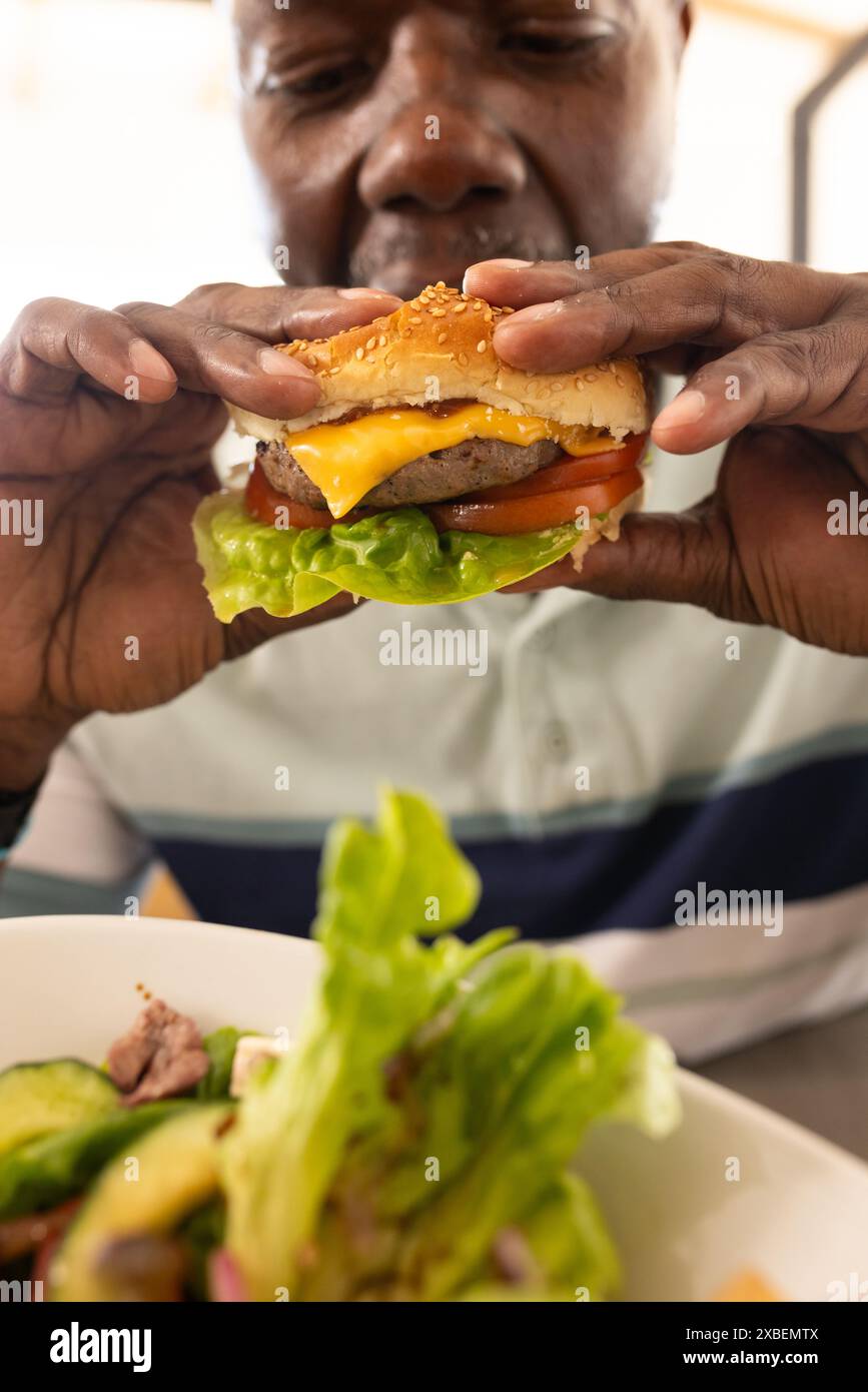 Mature African American man enjoying cheeseburger with fresh vegetables ...