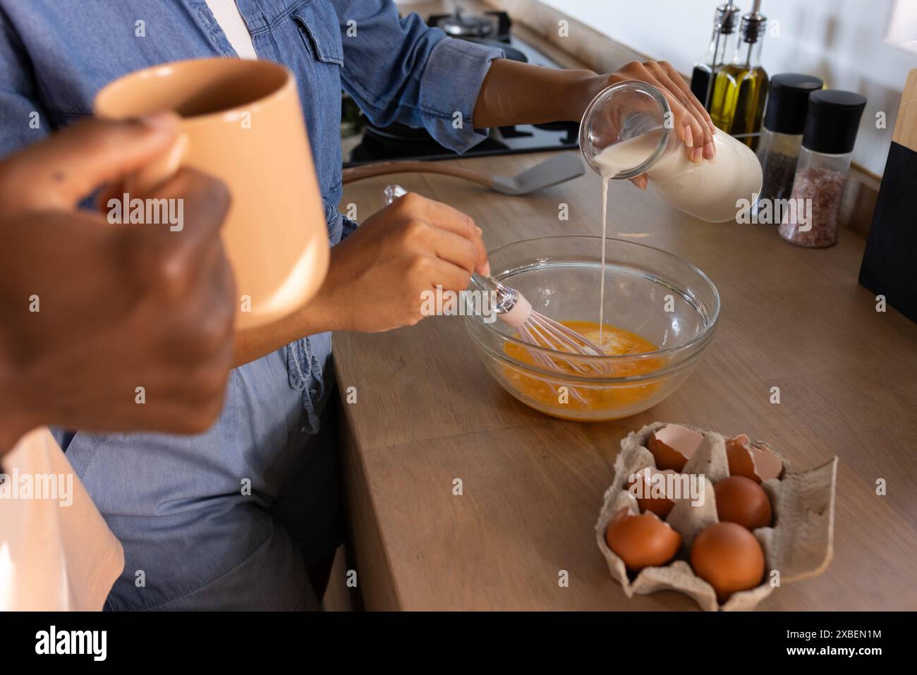 A diverse couple prepares breakfast, whisking eggs and adding milk ...