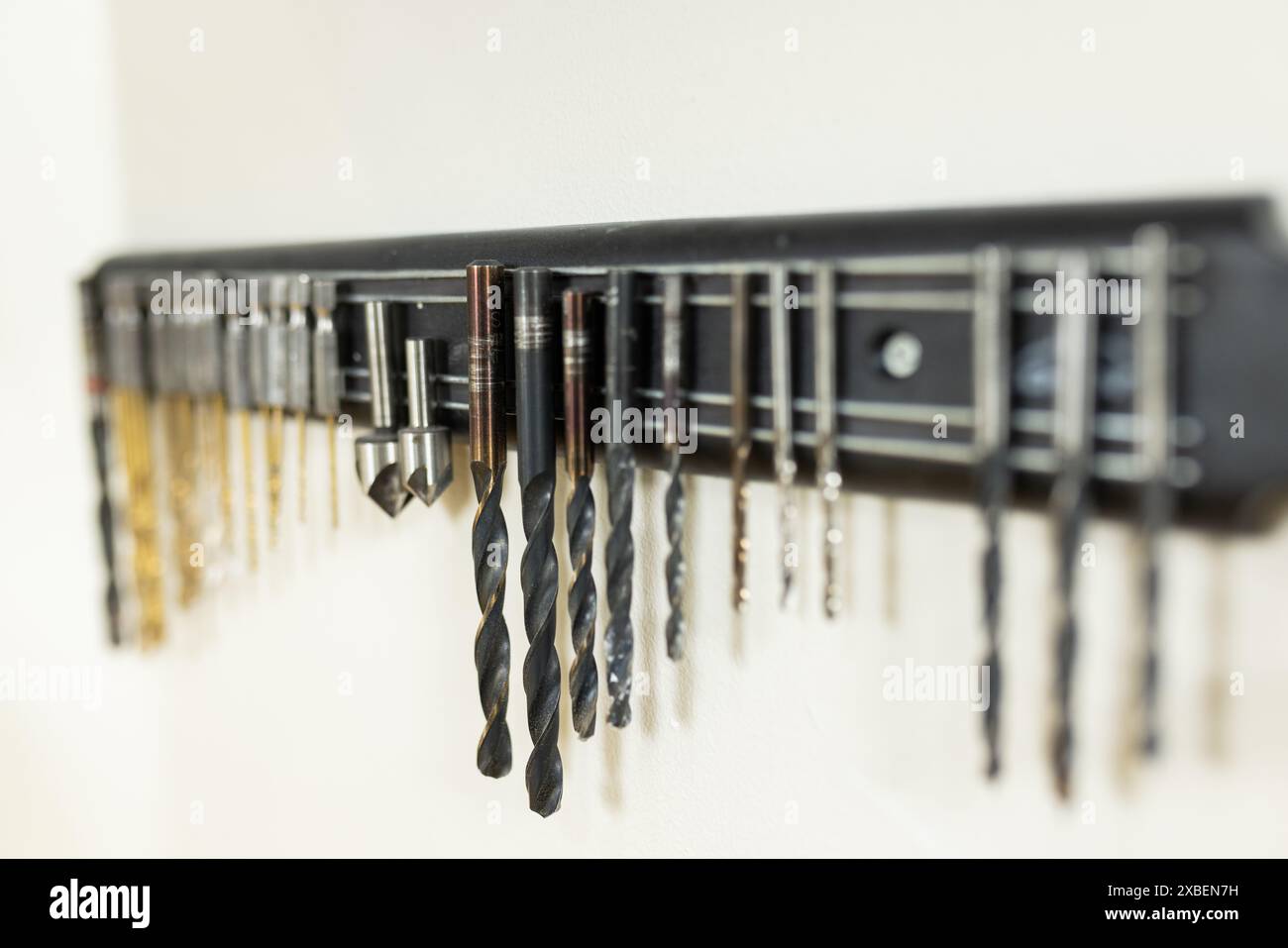 A row of various drill bits neatly organized on wall-mounted rack ...
