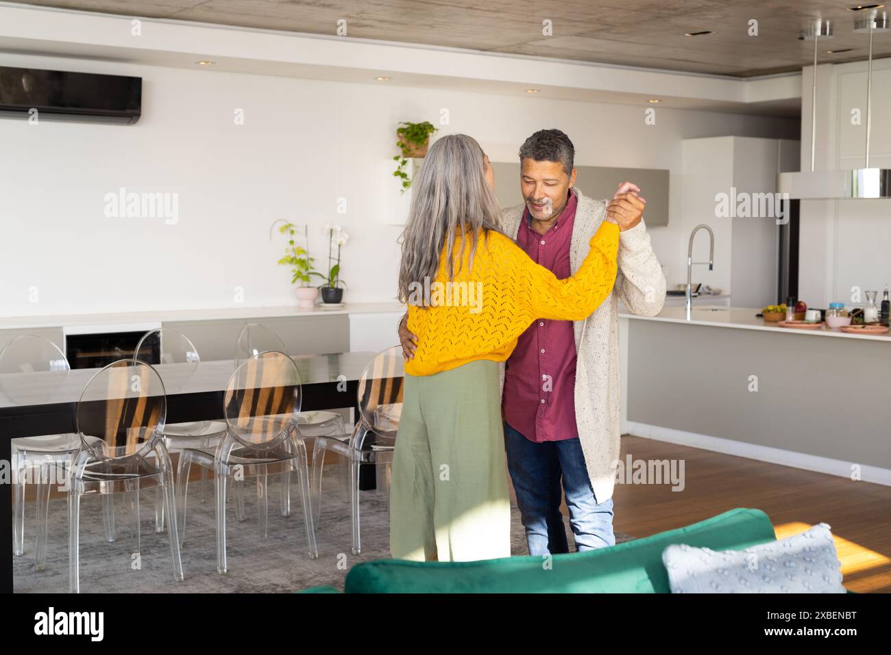 A biracial mature couple is dancing together in their living room, at ...