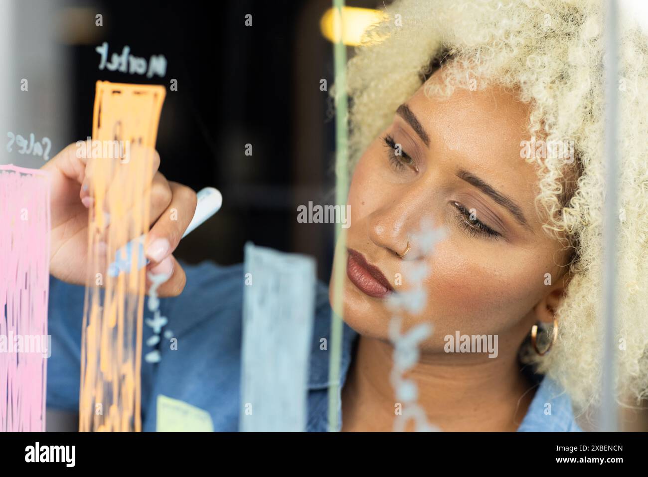 Biracial young woman writing on transparent board with marker in ...