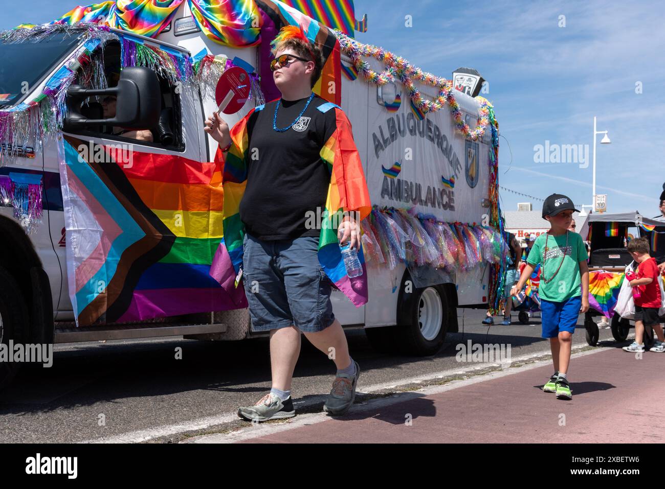 A boy adorned with rainbow colors walks next to an ambulance decorated ...