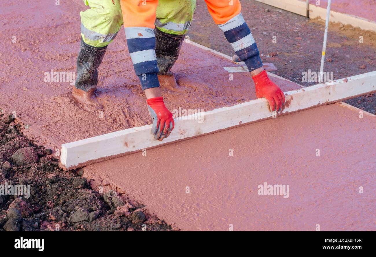 Builders pouring and levelling wet ready-mix concrete into formwork ...