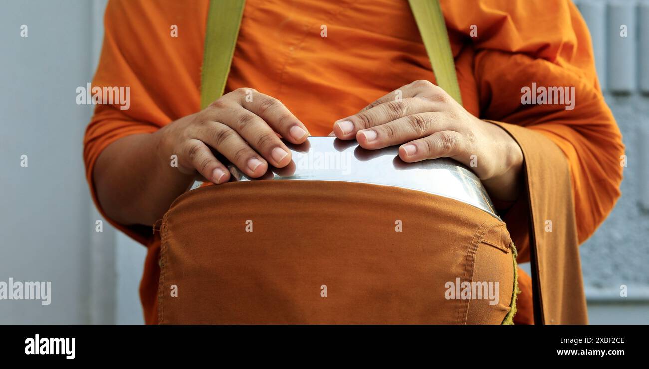 hand of monk dressing orange robe, holding bowl during reception of ...