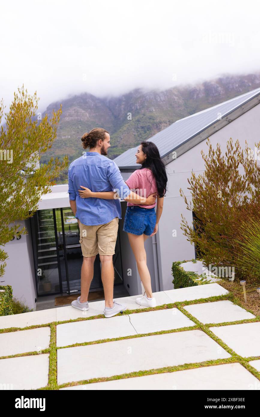 Diverse couple embrace while looking at their modern home Stock Photo ...