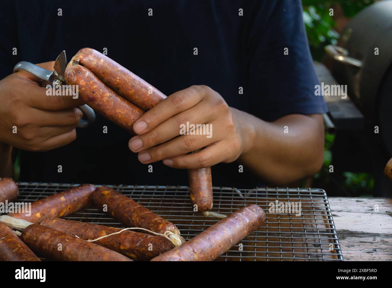 A man is cutting a sausage link that uses collagen casing, it will be ...