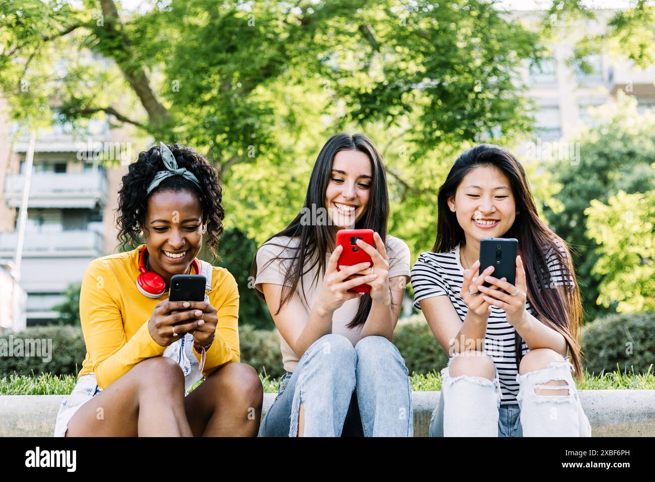Three multiracial women using mobile phone outdoors Stock Photo - Alamy