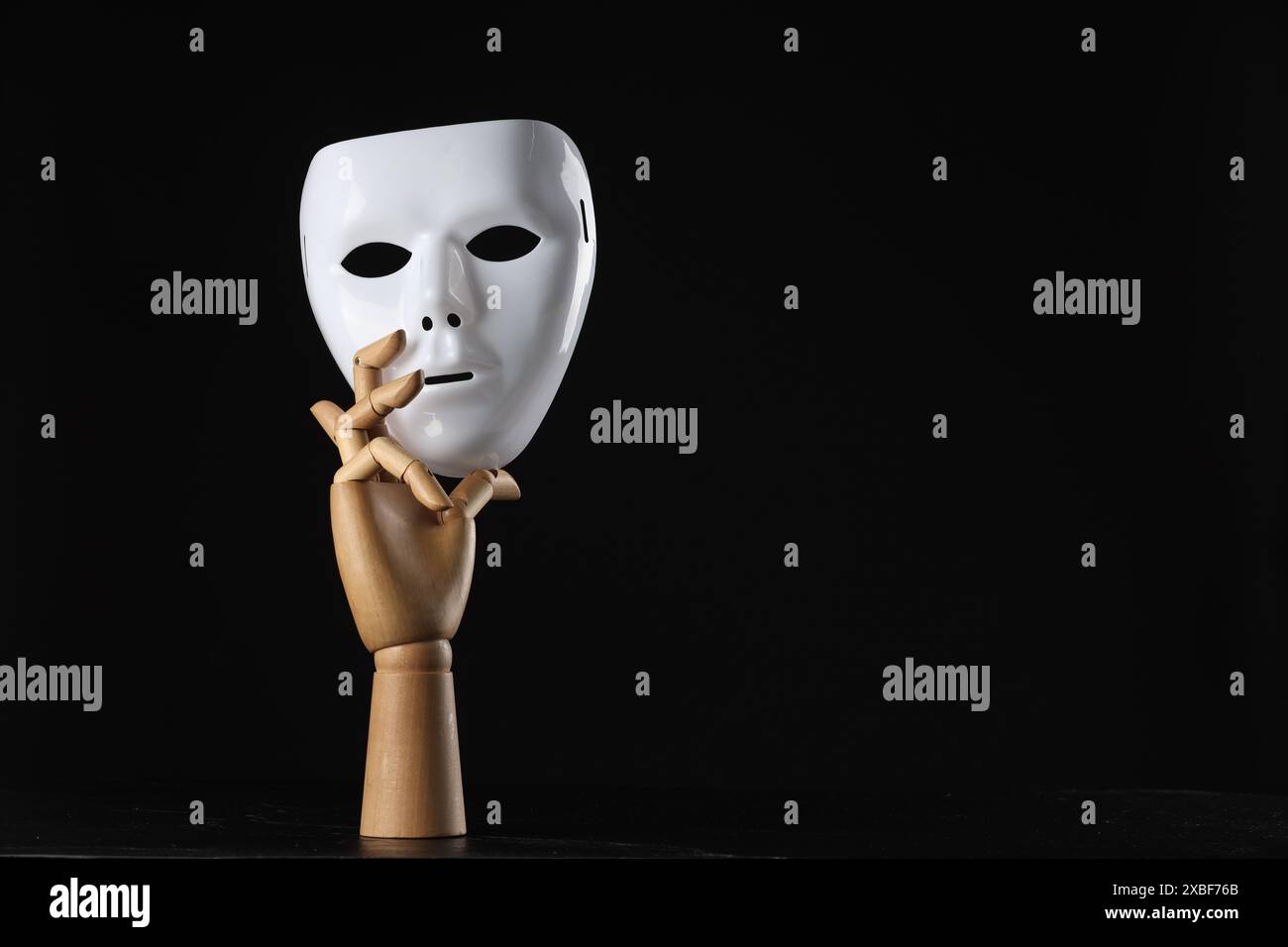 Wooden mannequin hand holding plastic mask on black background, space ...