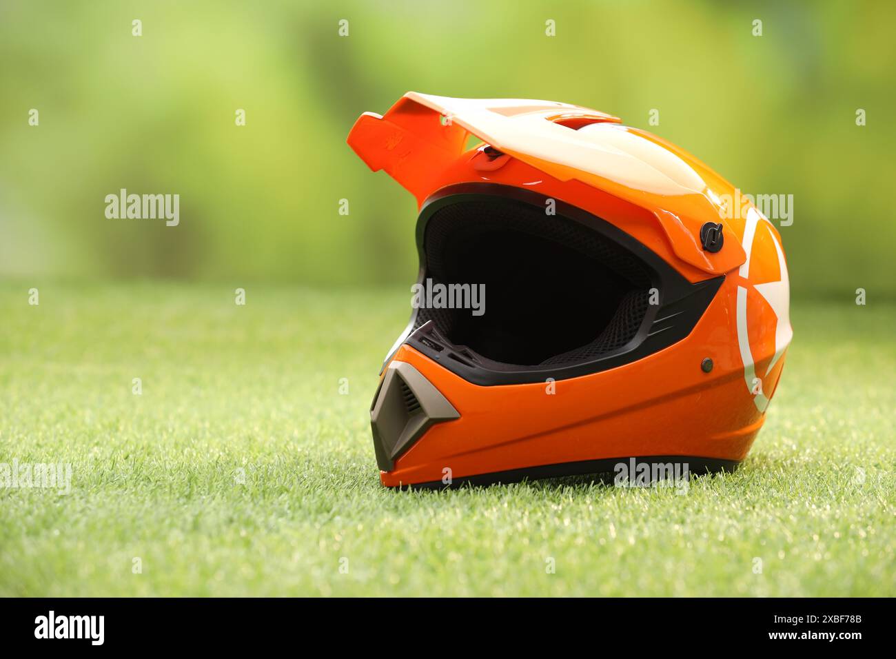 Orange motorcycle helmet with visor on green grass, space for text ...