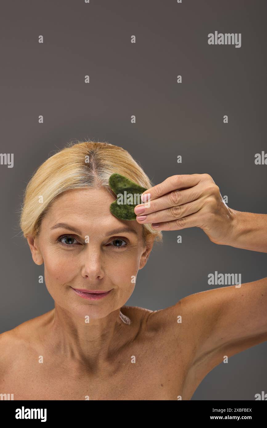 Lovely mature woman using gua sha on a gray backdrop Stock Photo - Alamy
