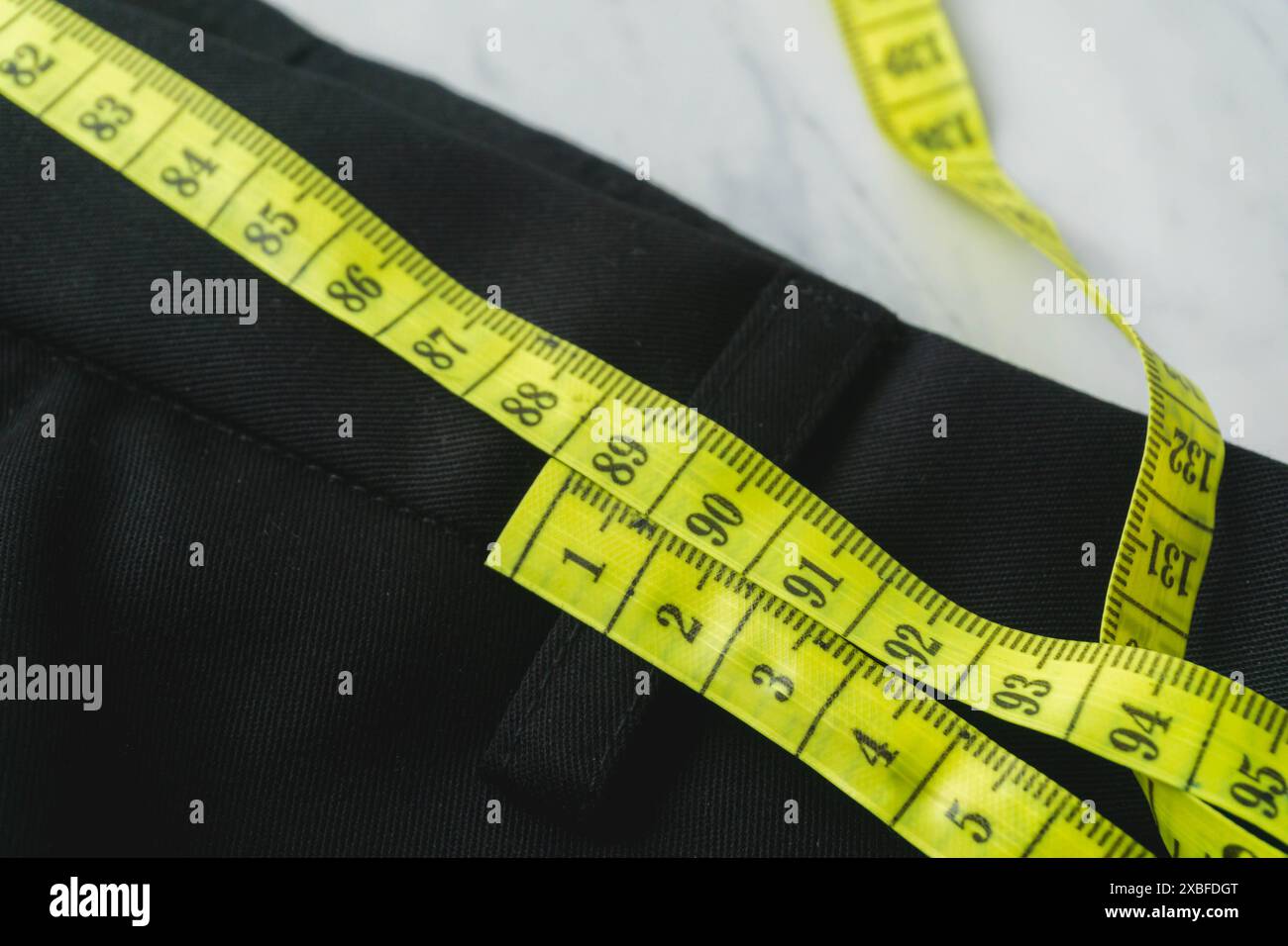 A black pair of pants is being measured by a yellow tape measure ...