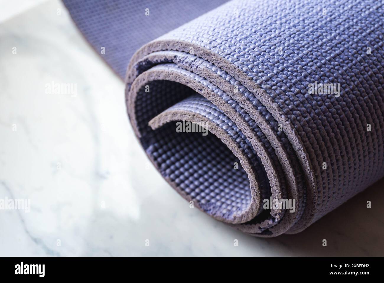 A yoga mat is rolled up on a marble countertop. The mat is purple and ...