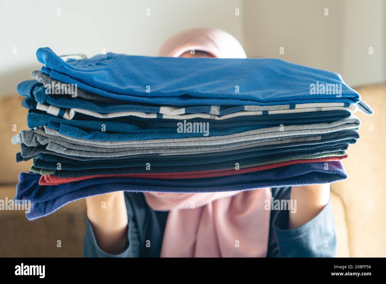 woman picking up stack of clothes that has finished ironed and folded ...