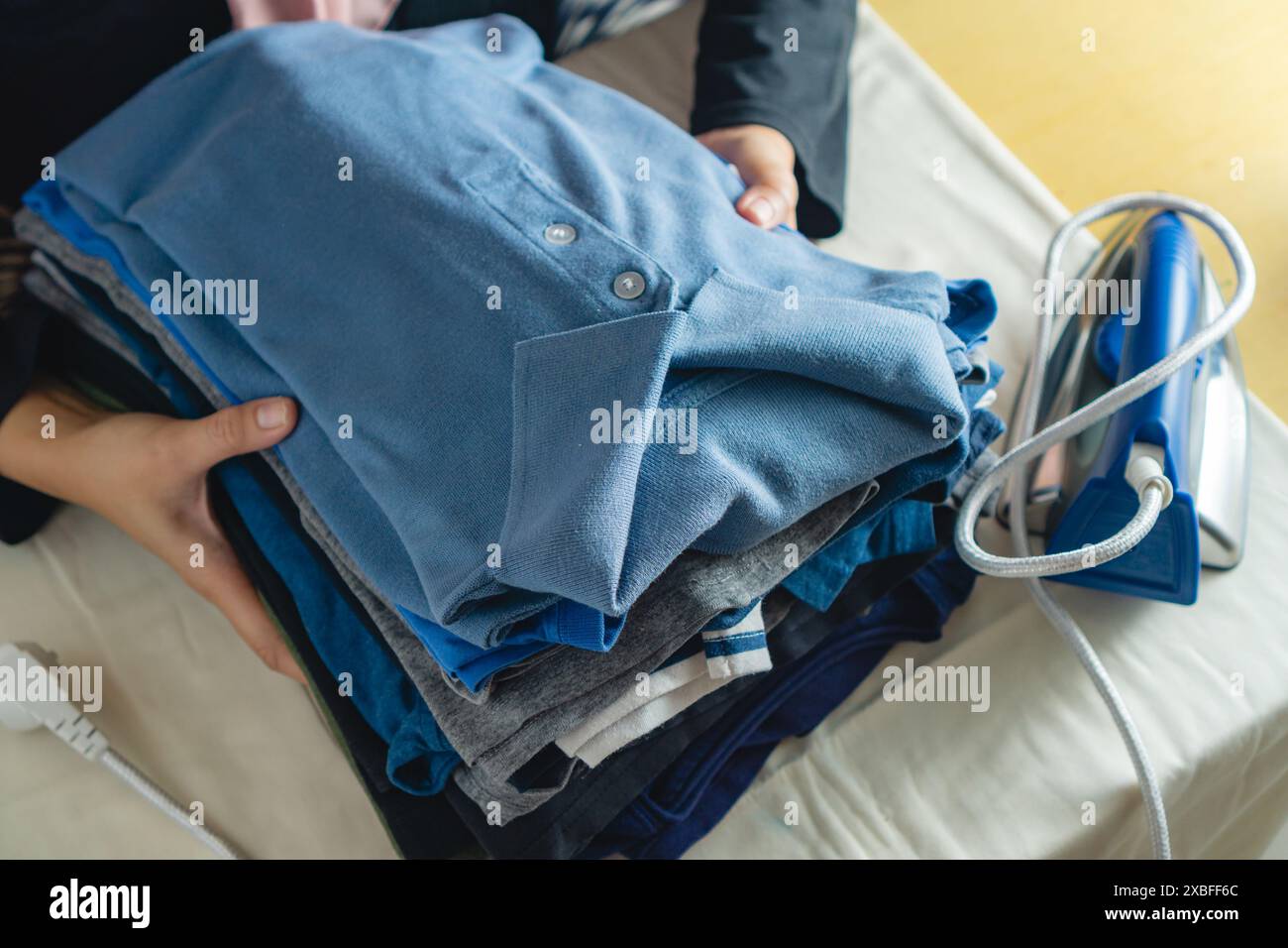 woman picking up stack of clothes that has finished ironed and folded ...
