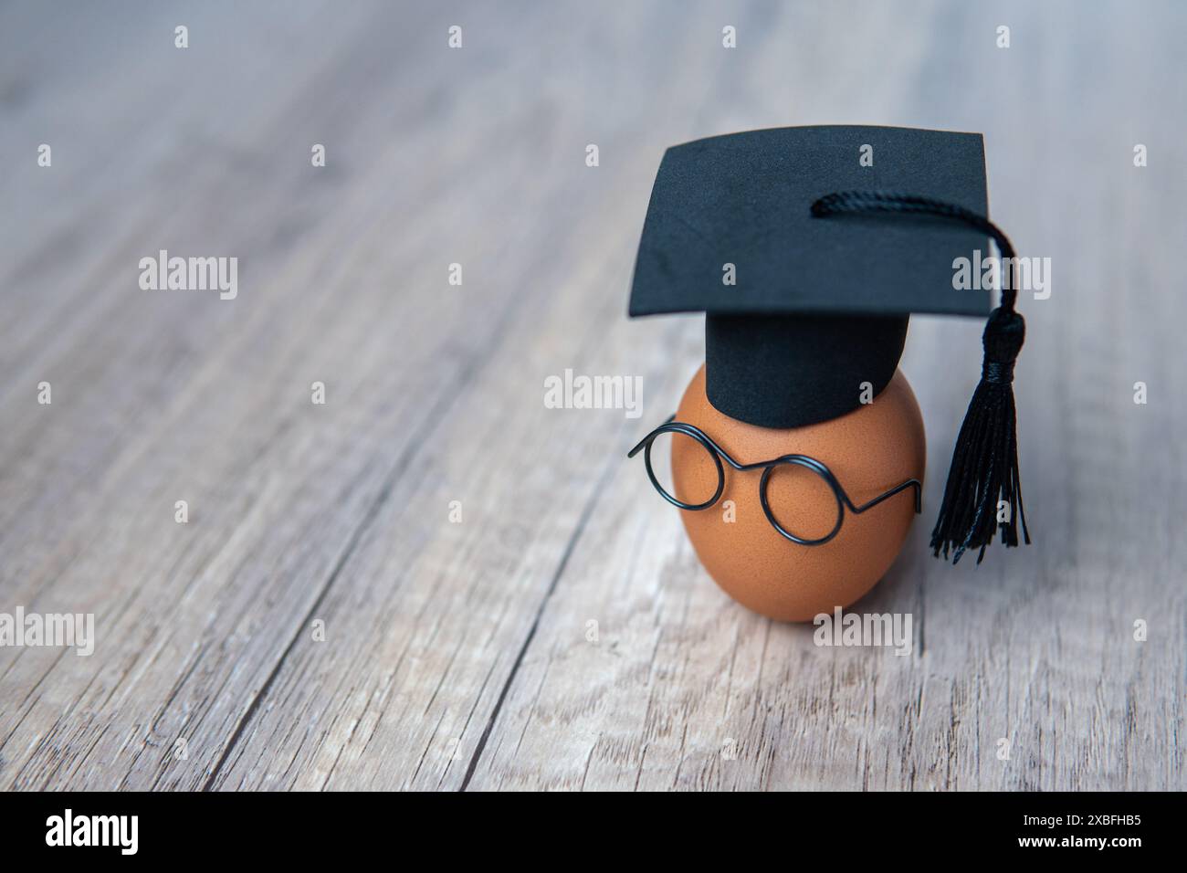 A close-up image of a brown egg wearing a black graduation cap and ...