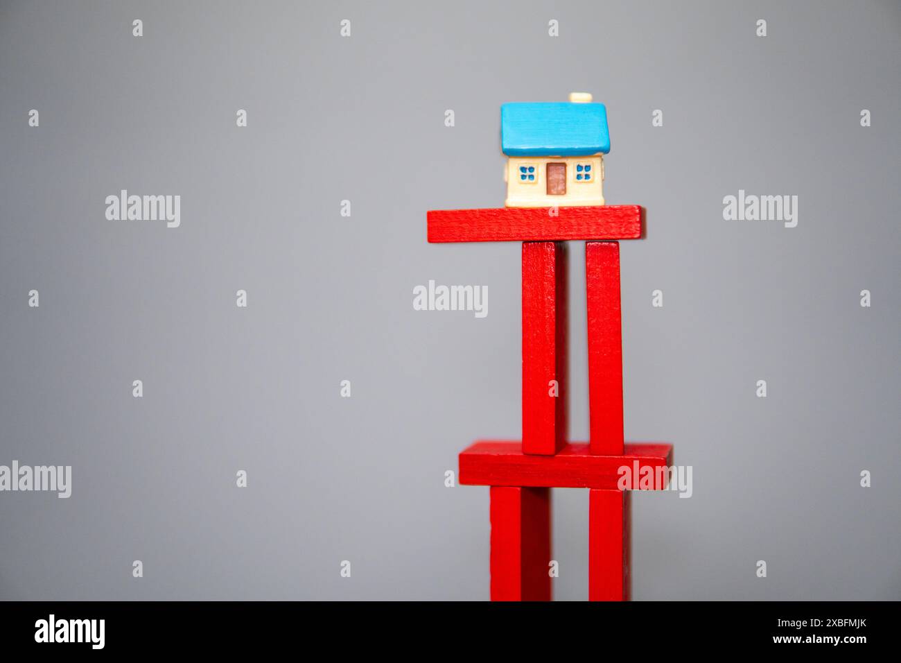 A close-up photo of a toy house on a precarious stack of red wooden ...