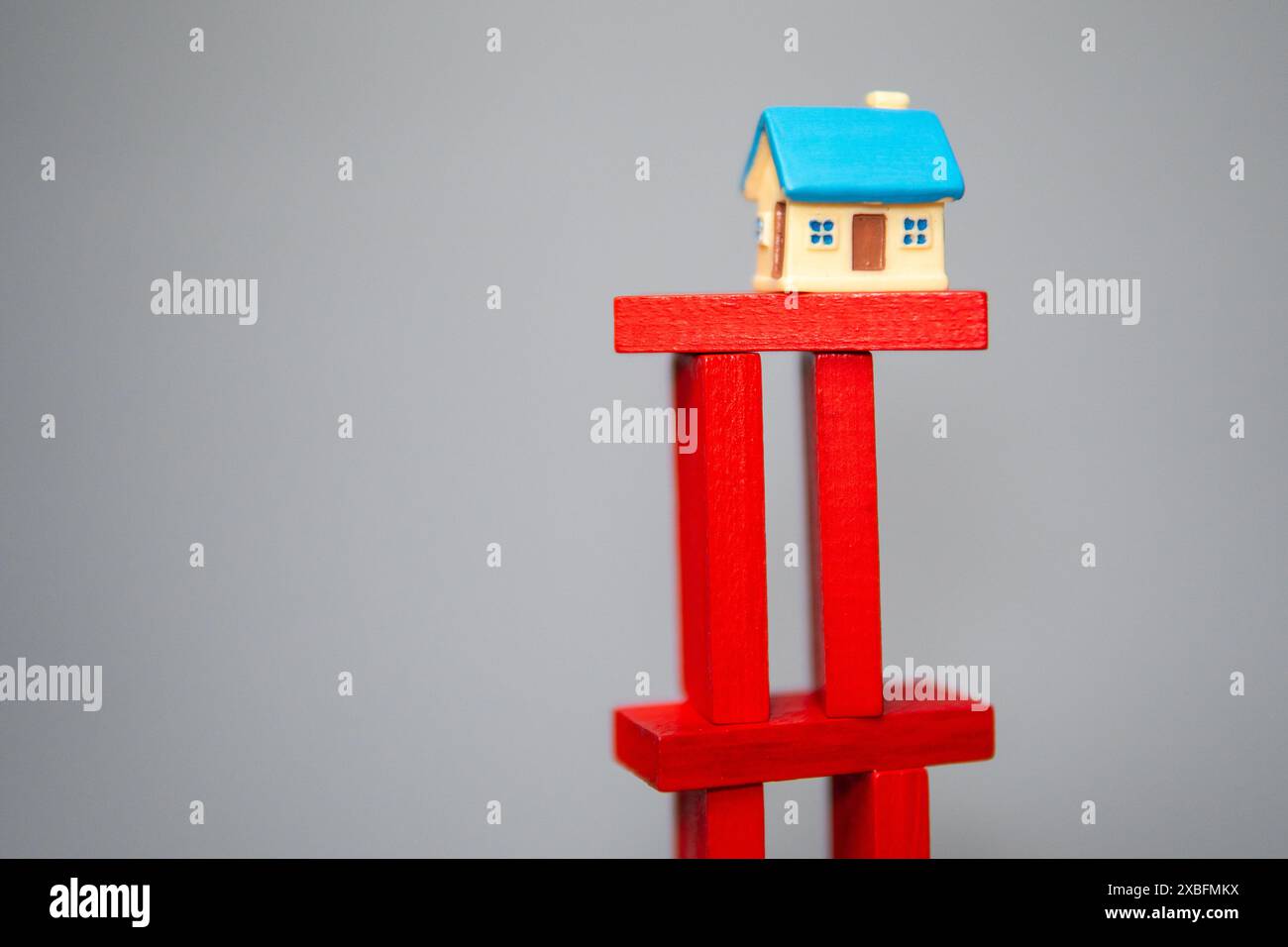 A close-up photo of a toy house on a precarious stack of red wooden ...