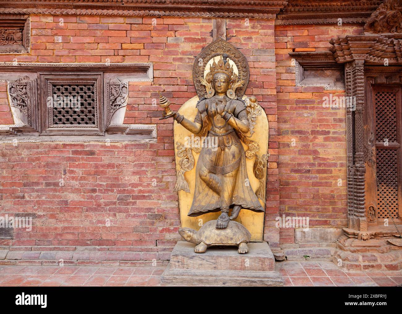 A detailed statue of a deity in front of a brick wall in Patan Durbar ...