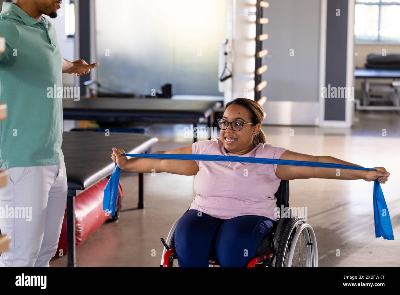 Quadriplegic biracial woman in wheelchair exercising with resistance band, copy space. She is in ...