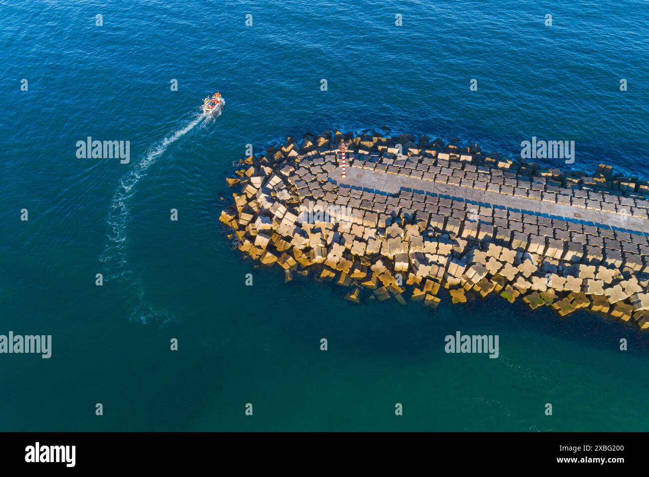 aerial zenithal view of a fishing boat leaving a harbor protected by ...