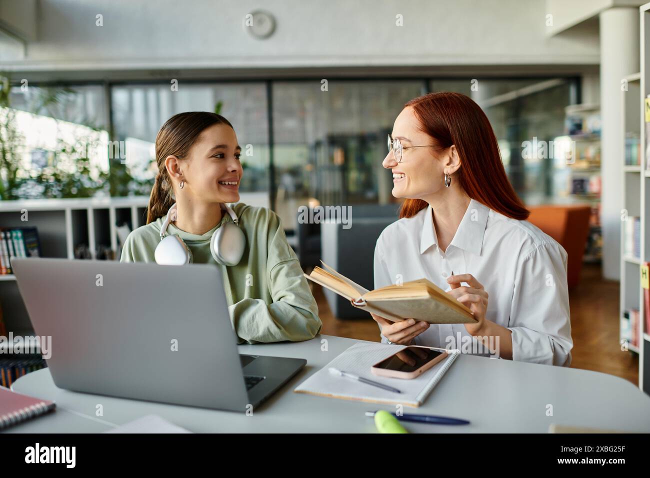 A redhead woman is teaching a teenage girl at a table while both are ...