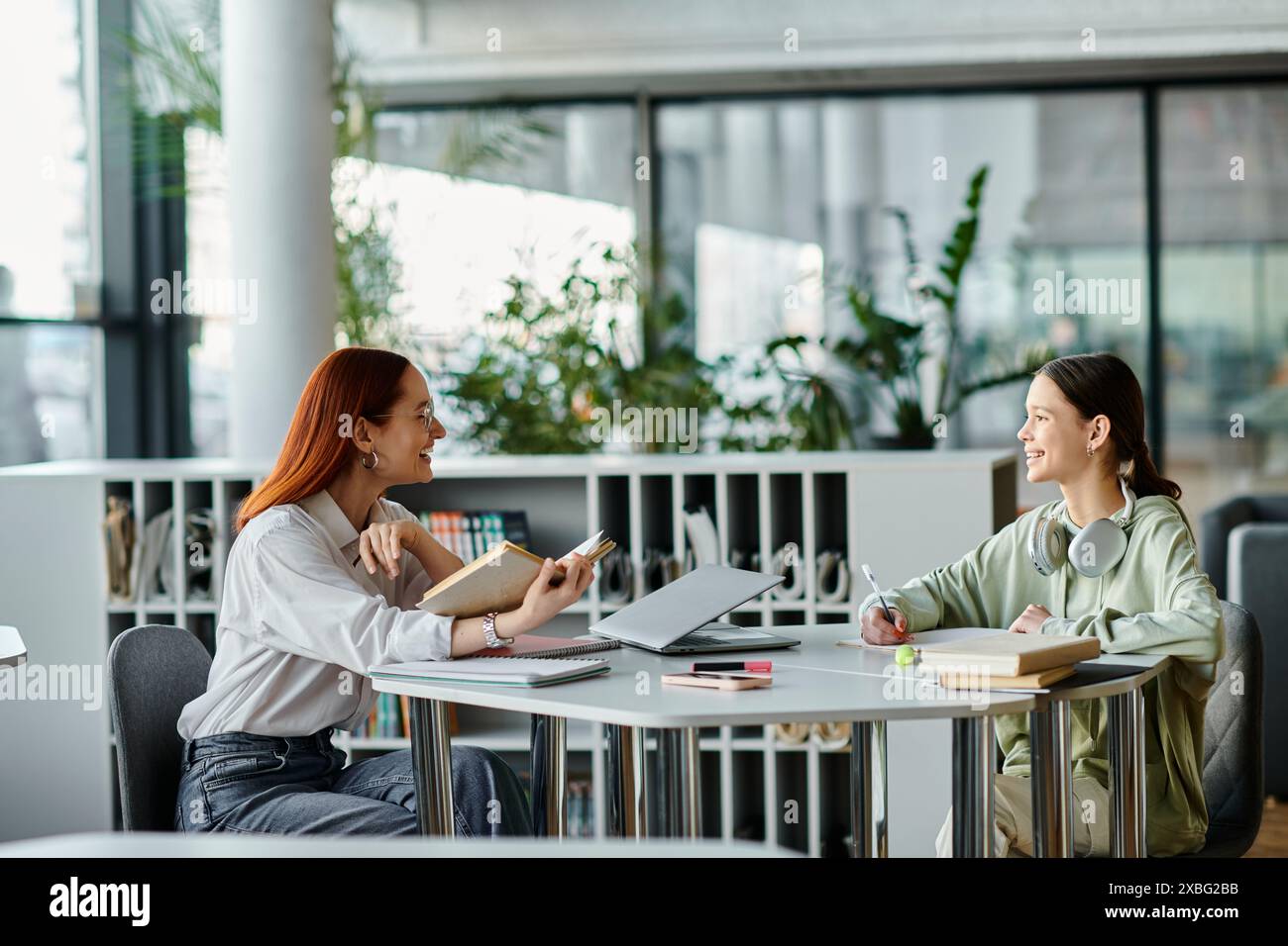 A redhead woman is tutoring a teenage girl at a table in a modern ...