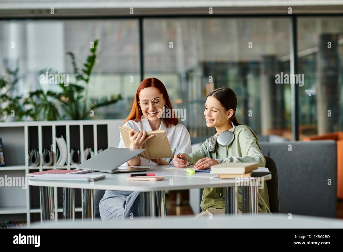 A redhead woman is tutoring a teenage girl at a table in an office ...