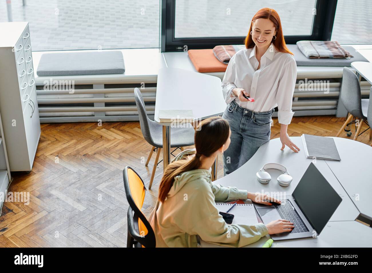 A tutor with red hair teaches a teenage girl in an office setting, both ...