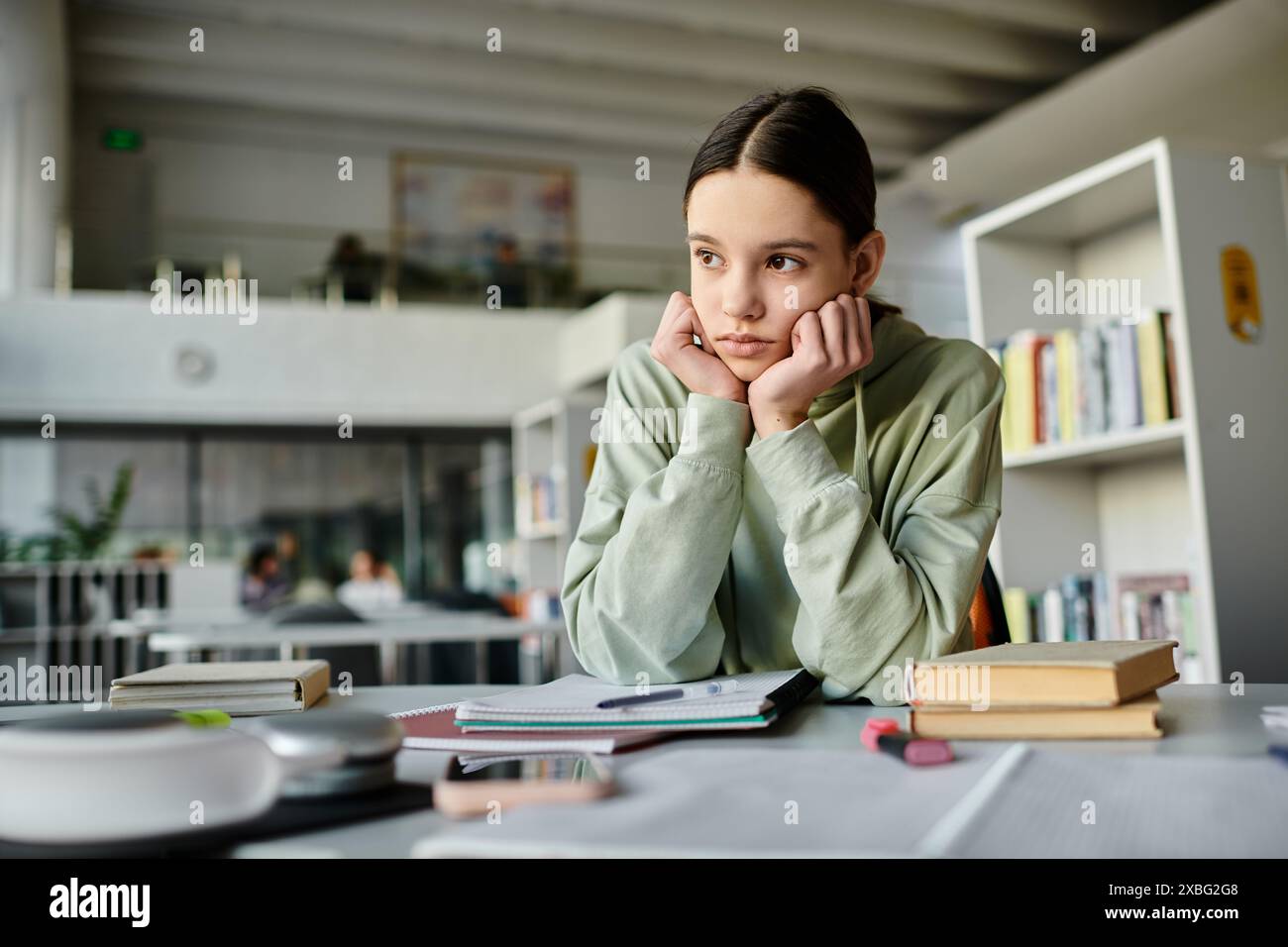 A teenage girl sits at a desk in an office, absorbed in doing homework ...