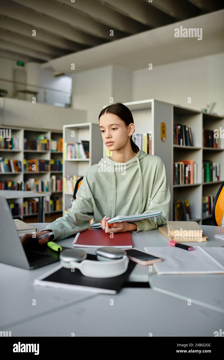 A teenage girl sits at a desk in a library, focusing intently on her ...