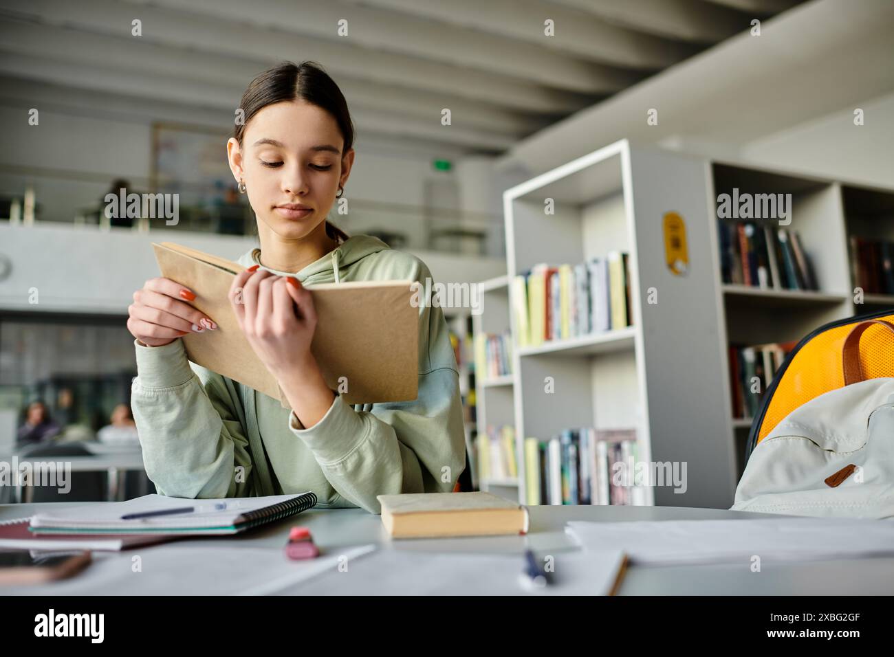 A teenage girl sits at a desk, writing diligently in a notebook ...