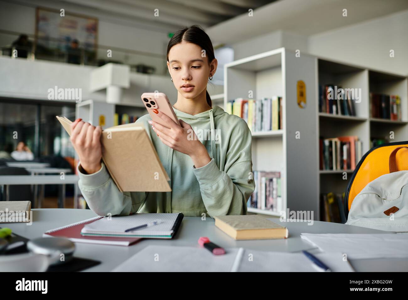 A teenage girl sits at a desk engrossed in a book while glancing at her ...