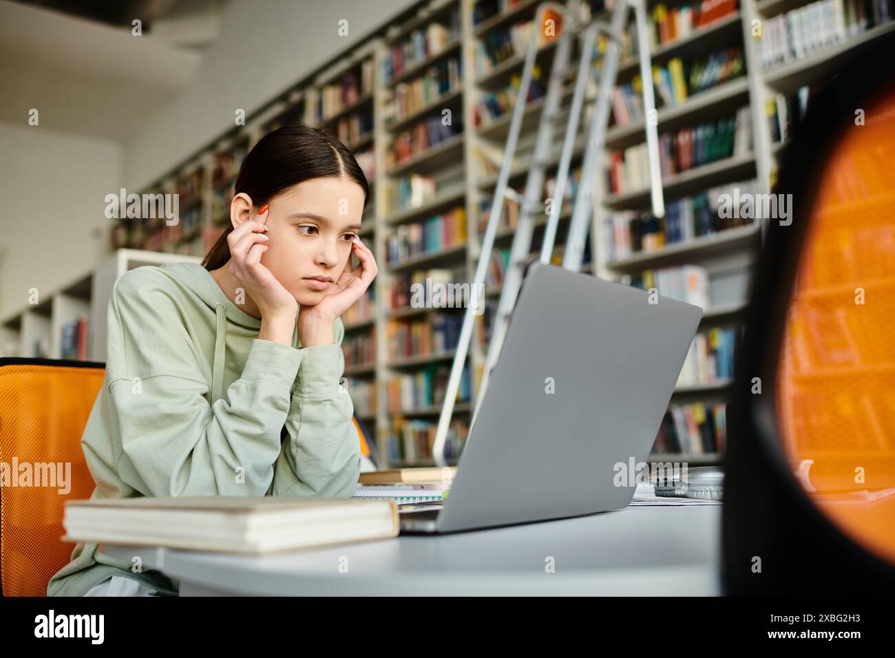 A teenage girl with a peaceful expression sits at a desk in a library ...