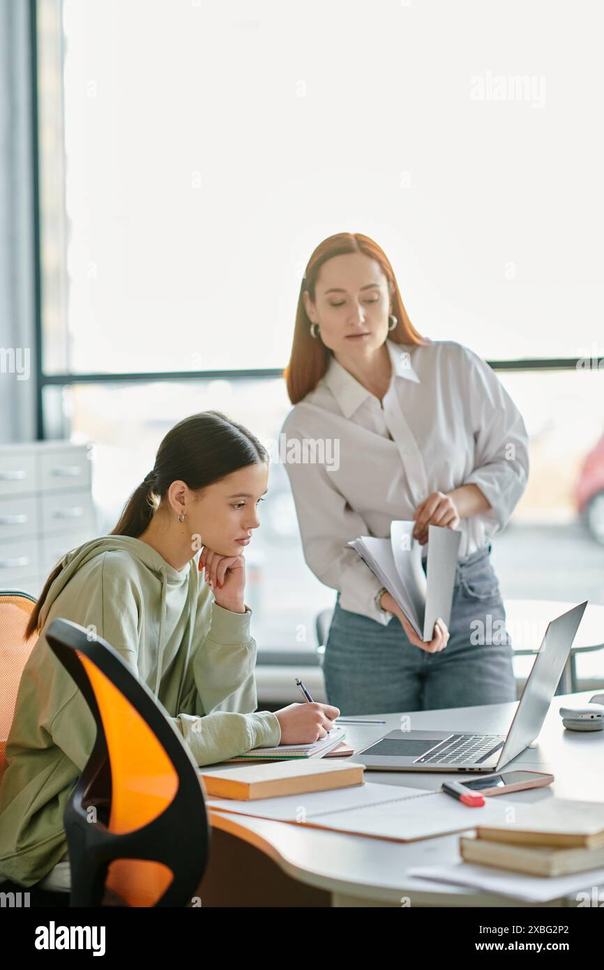A redhead tutor is teaching a teenage girl at a desk in an office ...