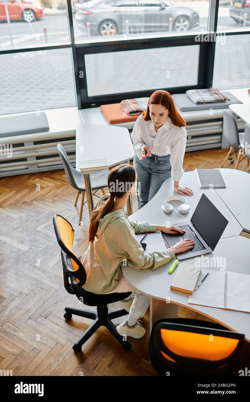 Redhead tutor teaching teenage girl in an office setting, both focused ...