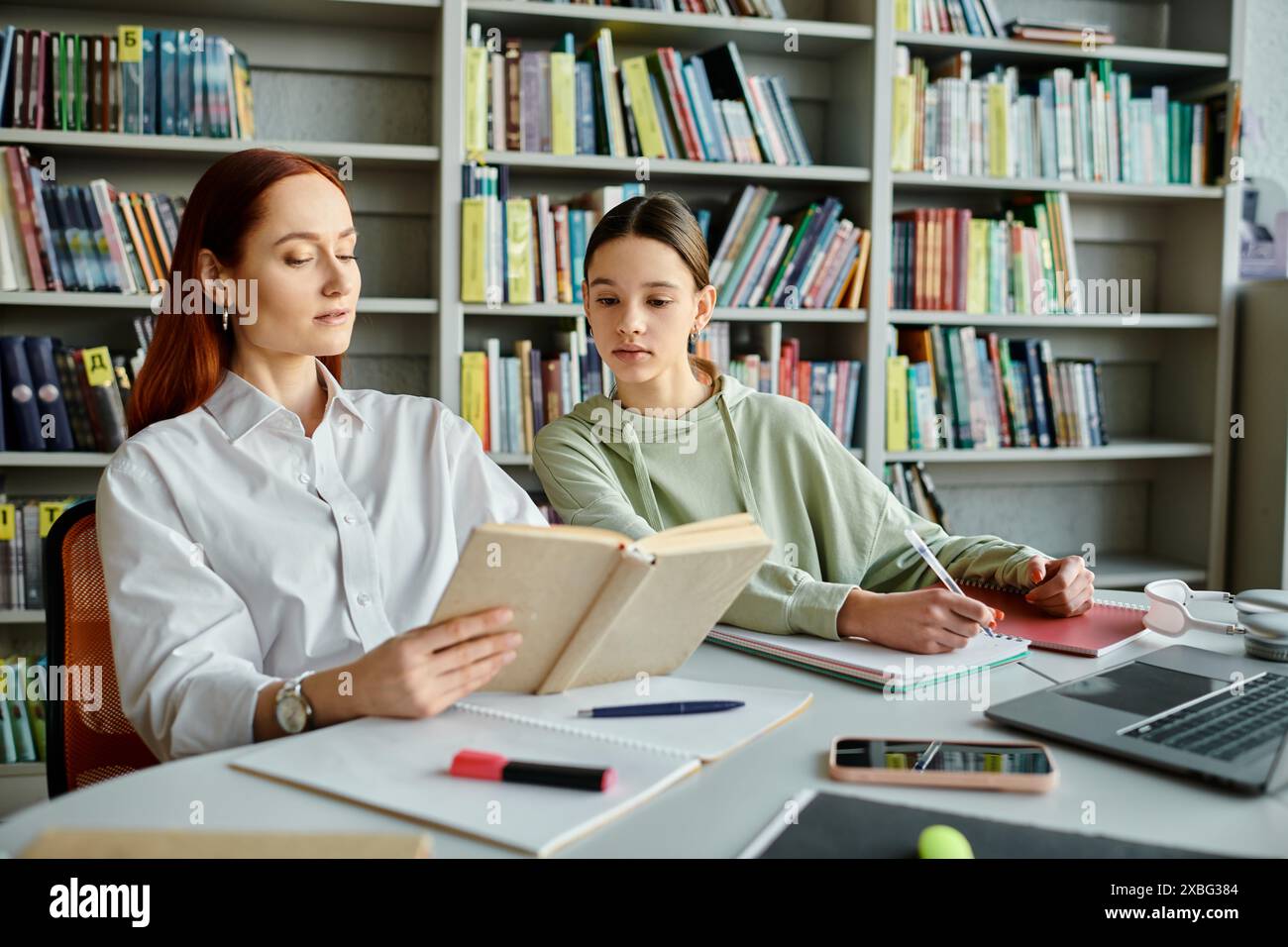 A tutor with red hair is teaching a teenage girl at a table in the ...