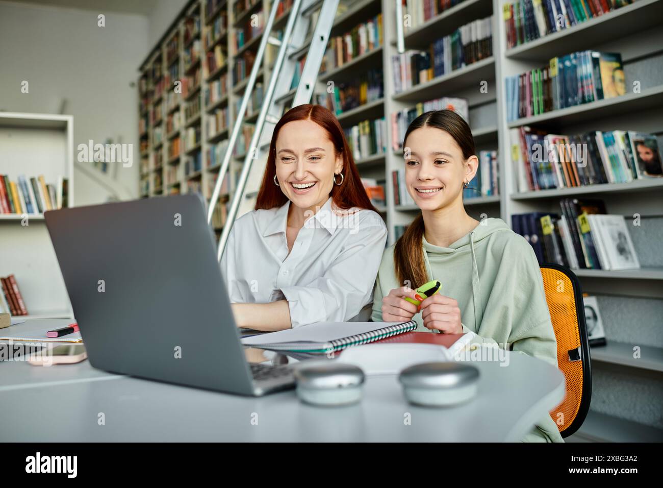 Redhead tutor teaches a teenage girl at a library table with laptops, engaging in after-school ...