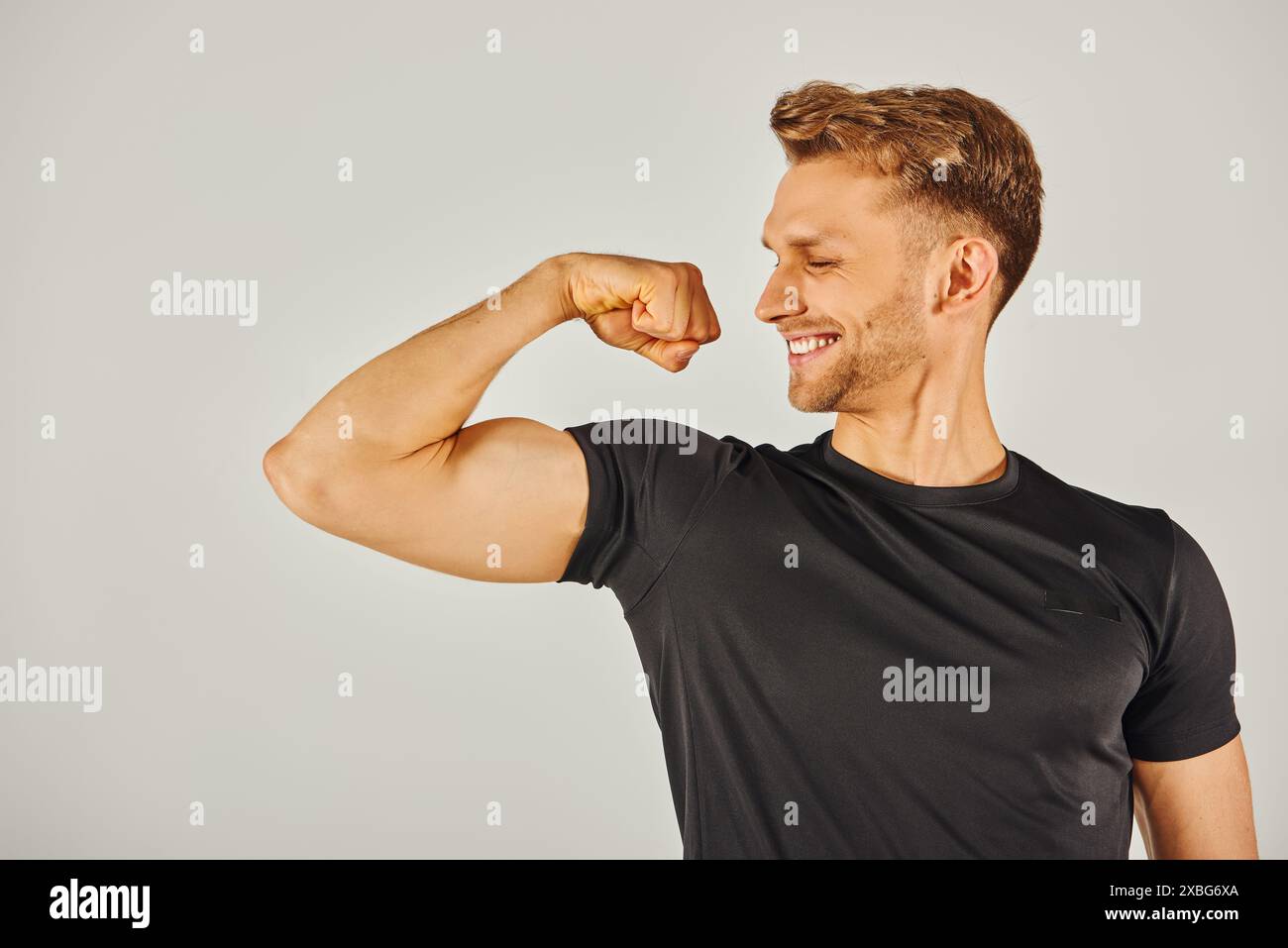A young athletic man in active wear flexes his biceps confidently ...