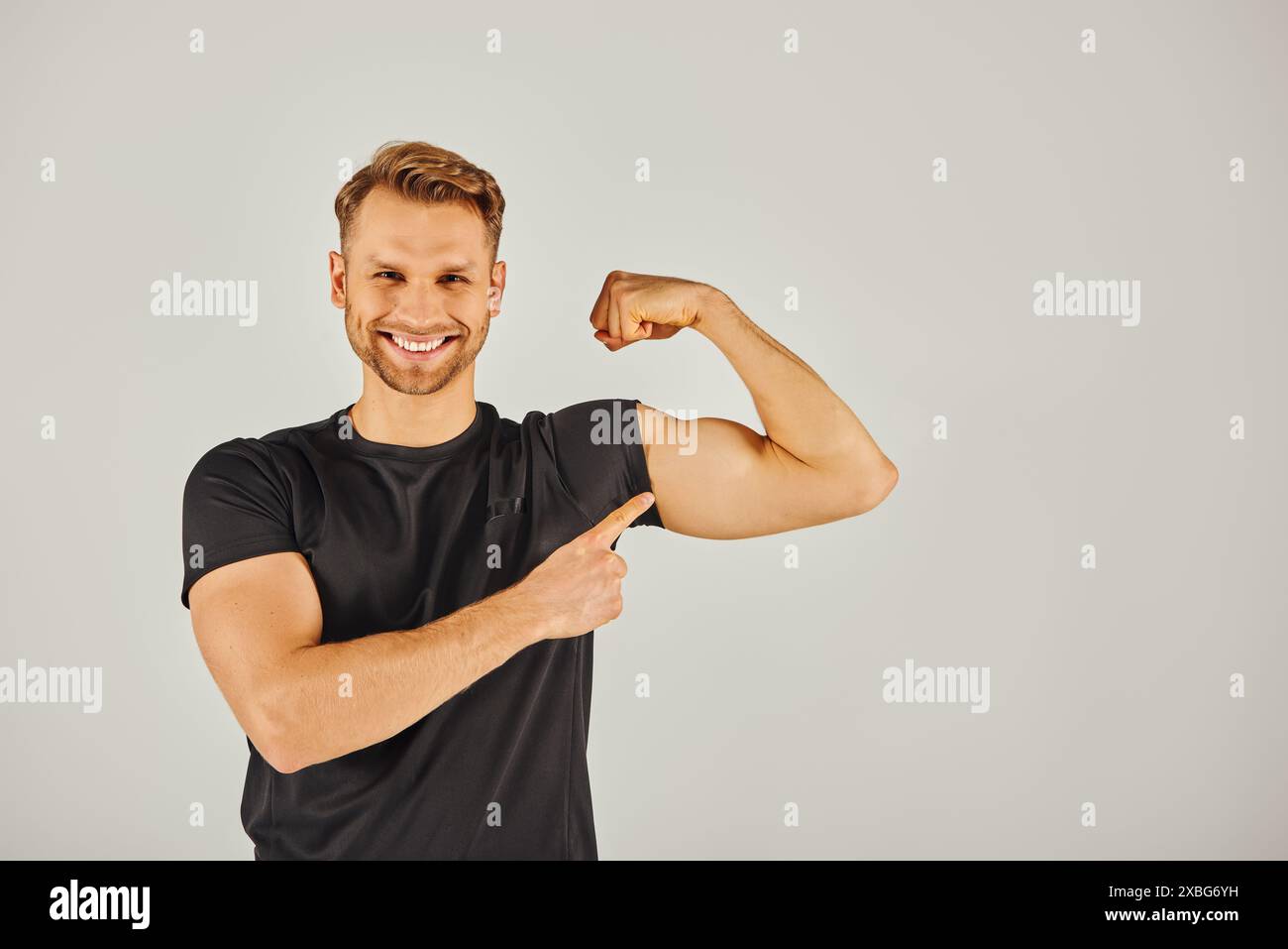 A young athletic man in active wear flexing his biceps against a gray ...