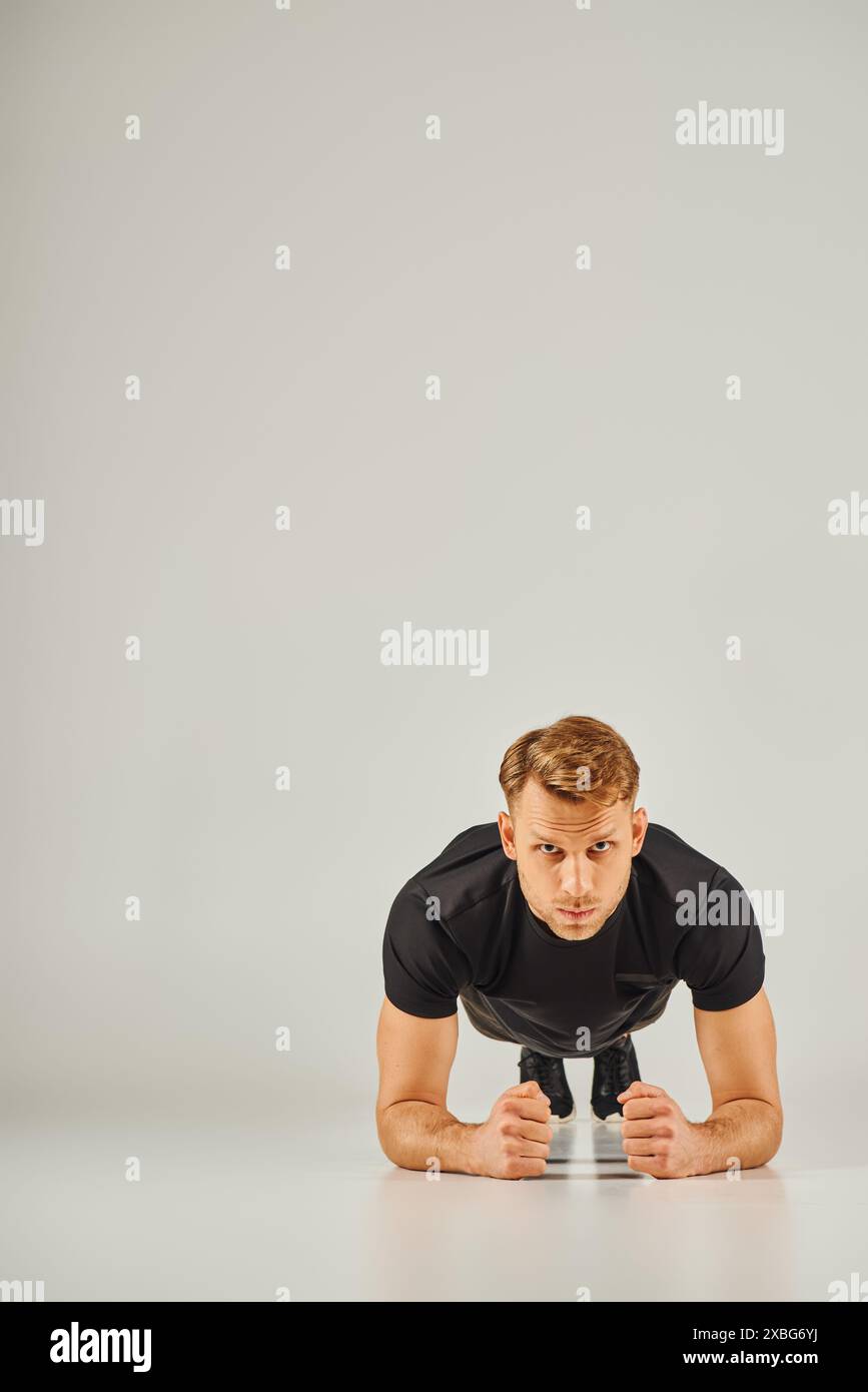 A young athletic man in active wear, performing push ups on a grey ...