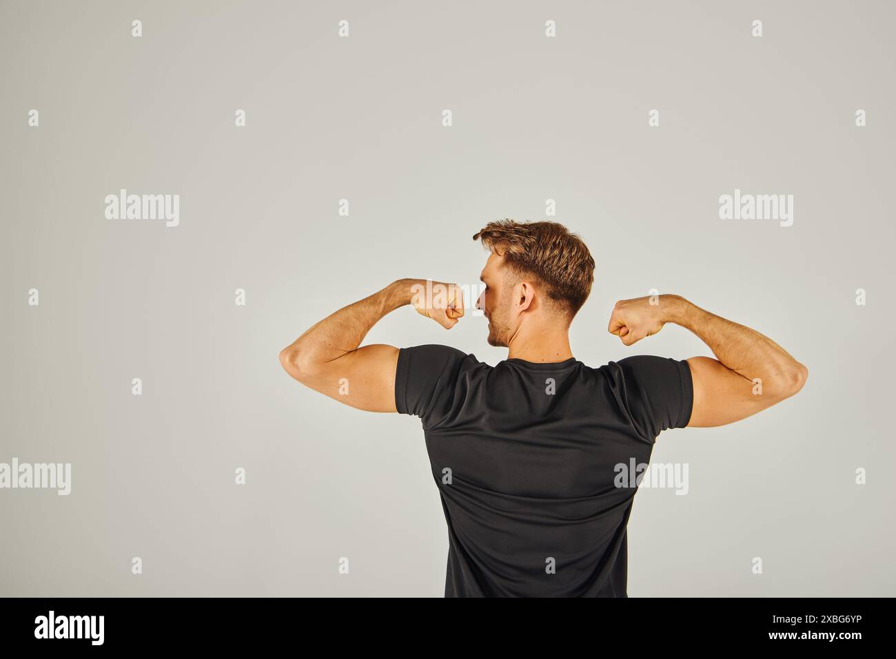 A young athletic man flexes his muscles in front of a white background ...