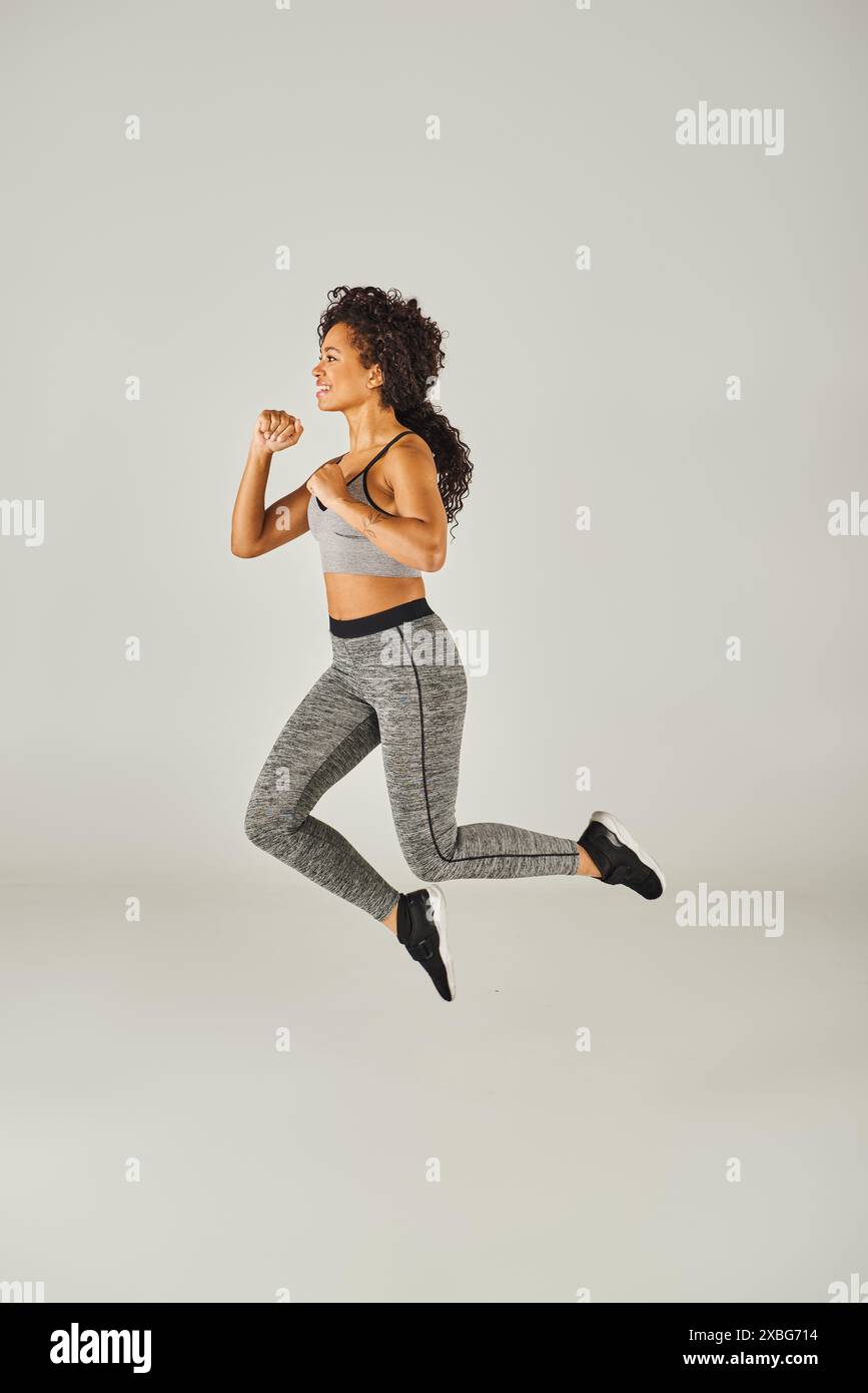 A young African American woman performs a dynamic jump in a grey sports ...
