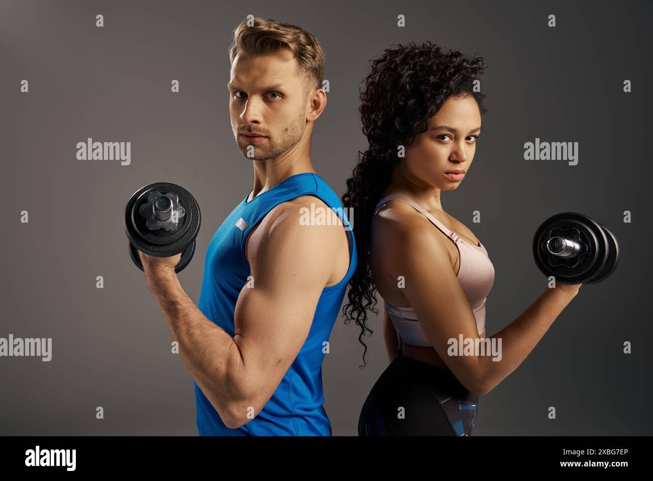 A fit and multicultural young couple poses confidently with dumbbells ...