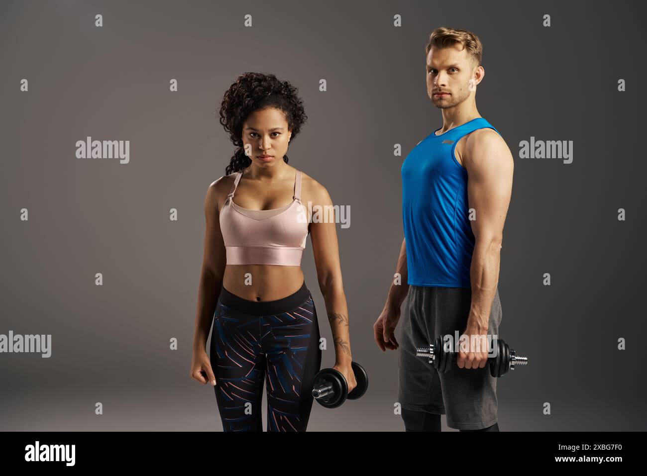 Multicultural fit couple in activewear strike poses with dumbbells ...