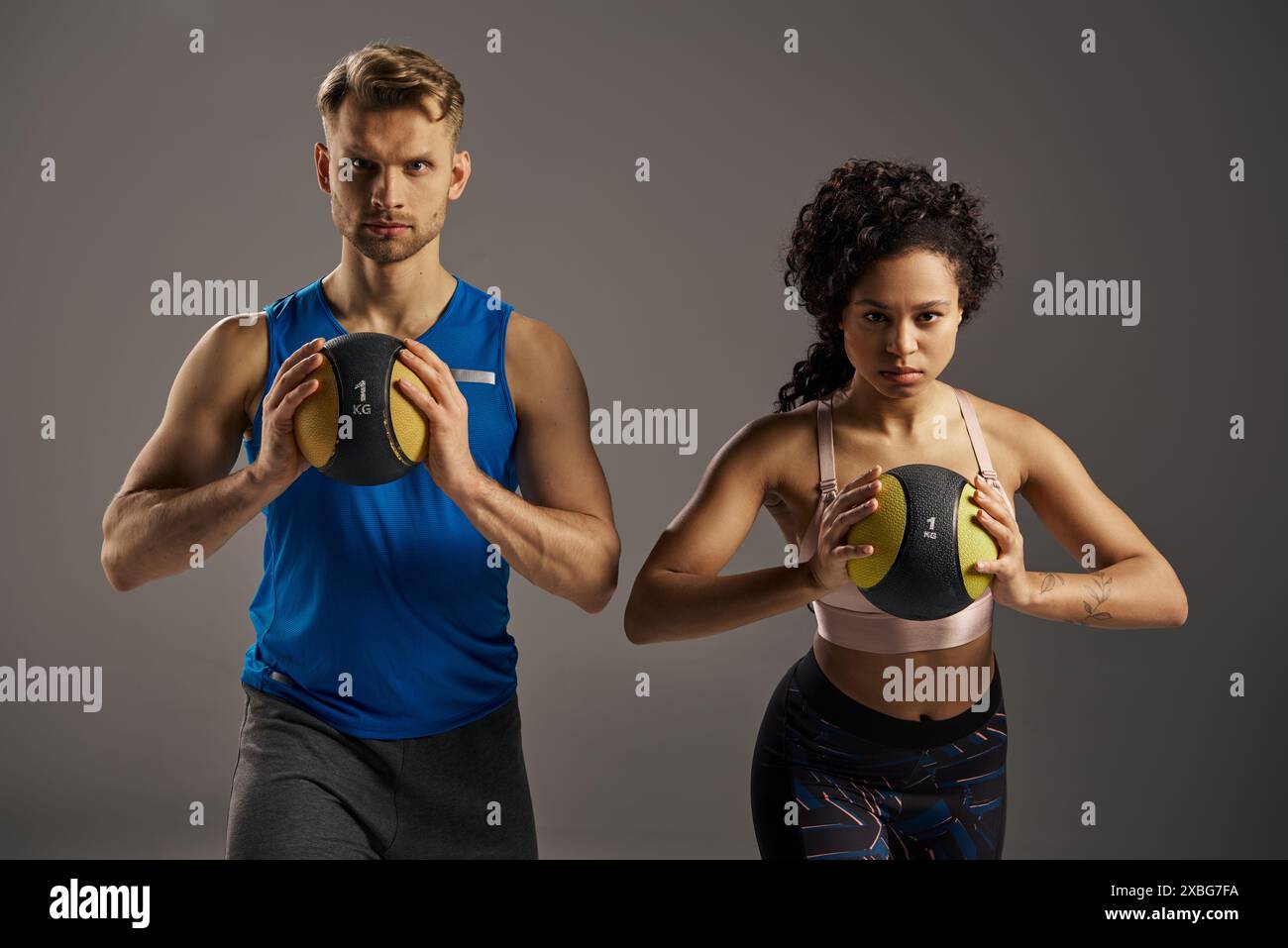 Young, fit man and woman in active wear lift balls together against a ...