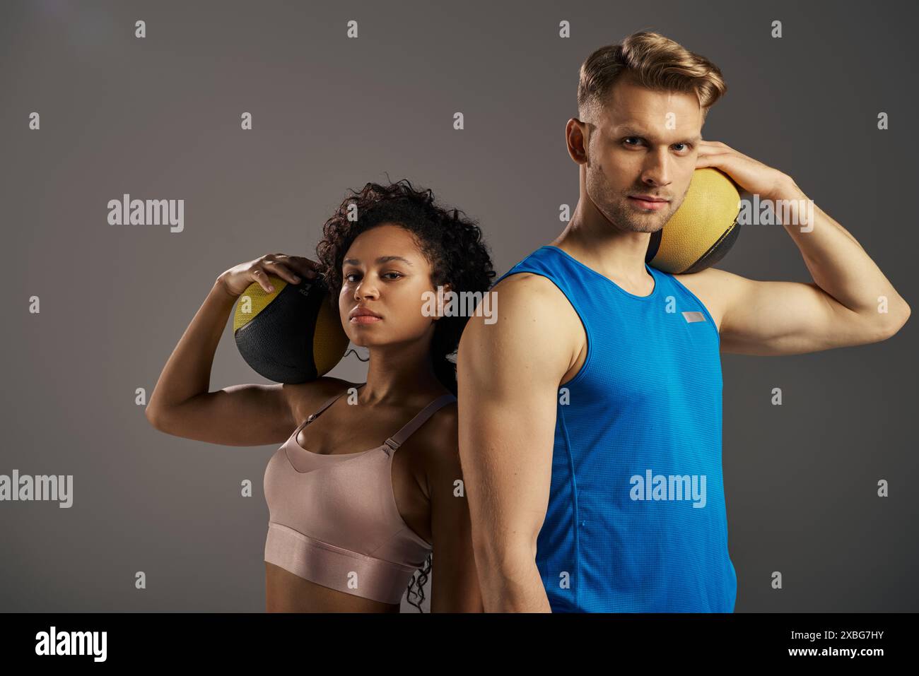 Young multicultural couple in active wear pose with balls in studio ...
