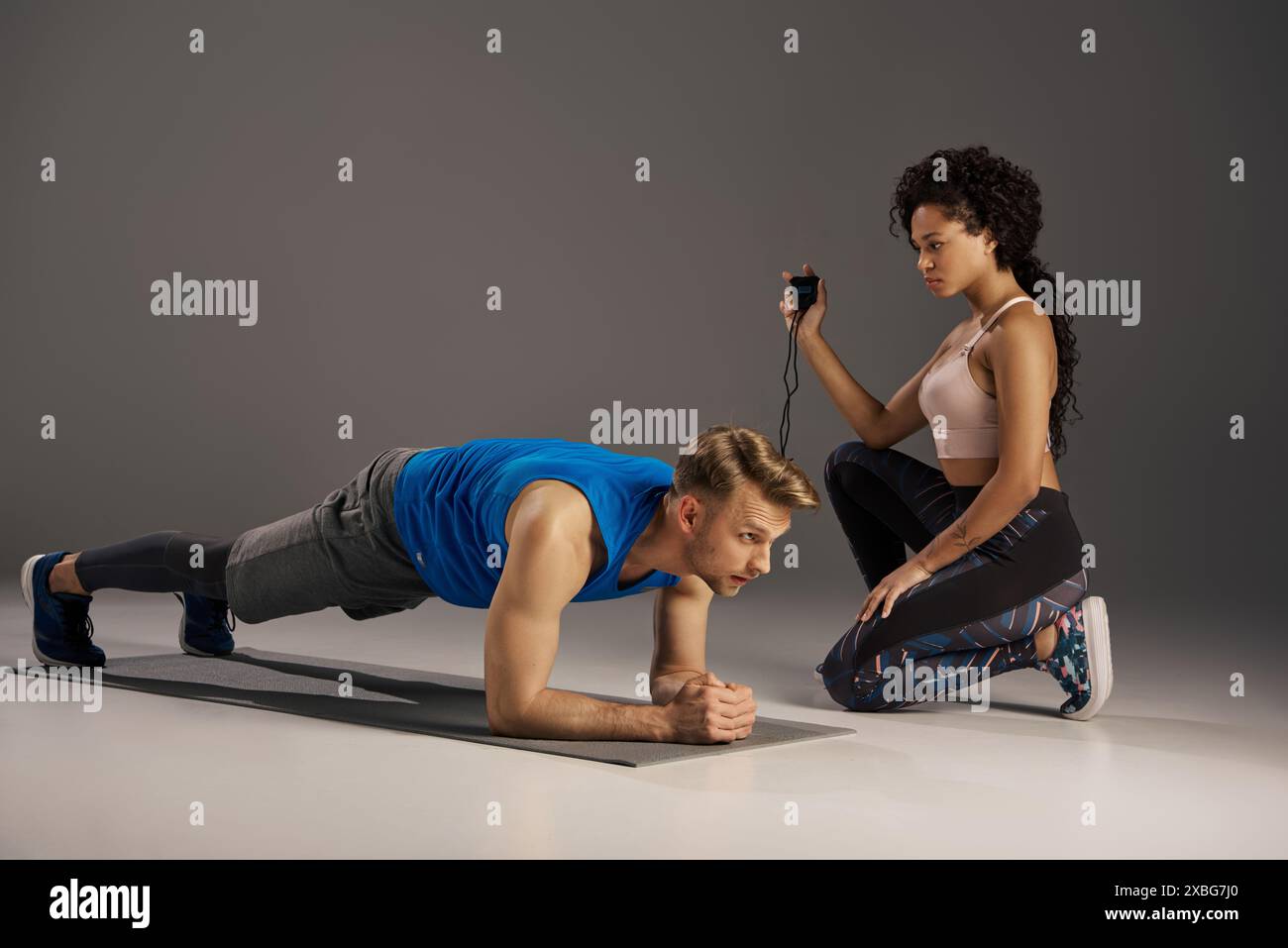 Young multicultural man and woman in active wear doing push ups on a plank in a studio ...