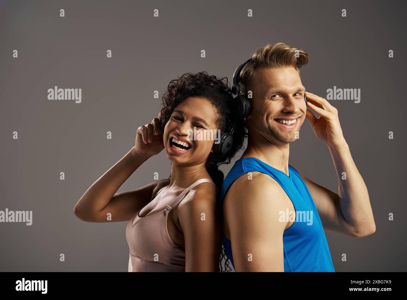 A young man and woman in activewear are immersed in music, listening through headphones with ...